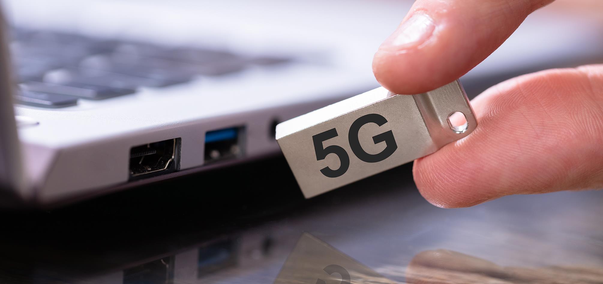 5g modem hålls mellan två fingrar brevid en laptop